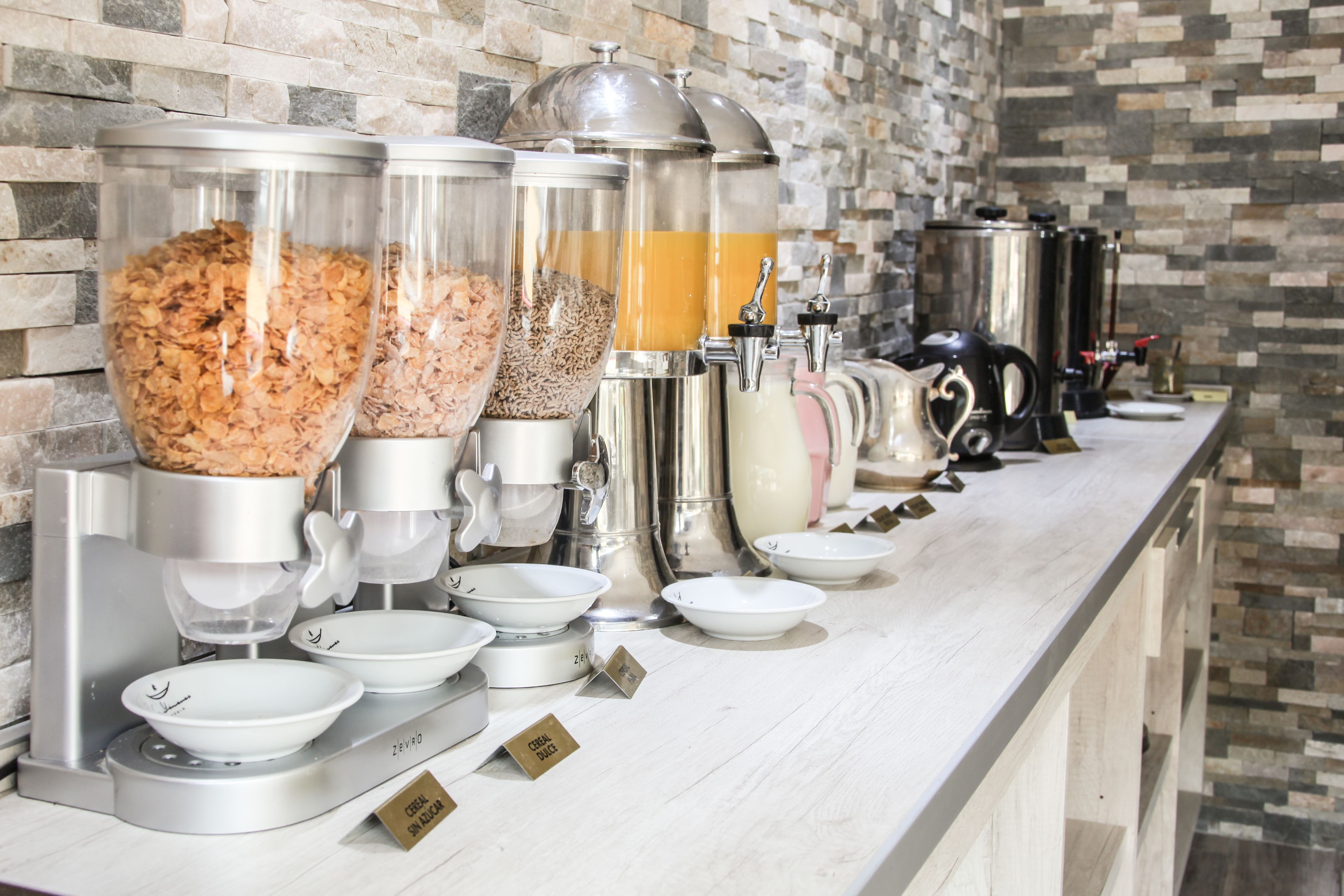 Uma mesa de pequeno-almoço com diversos dispensadores de comida e máquinas de café.