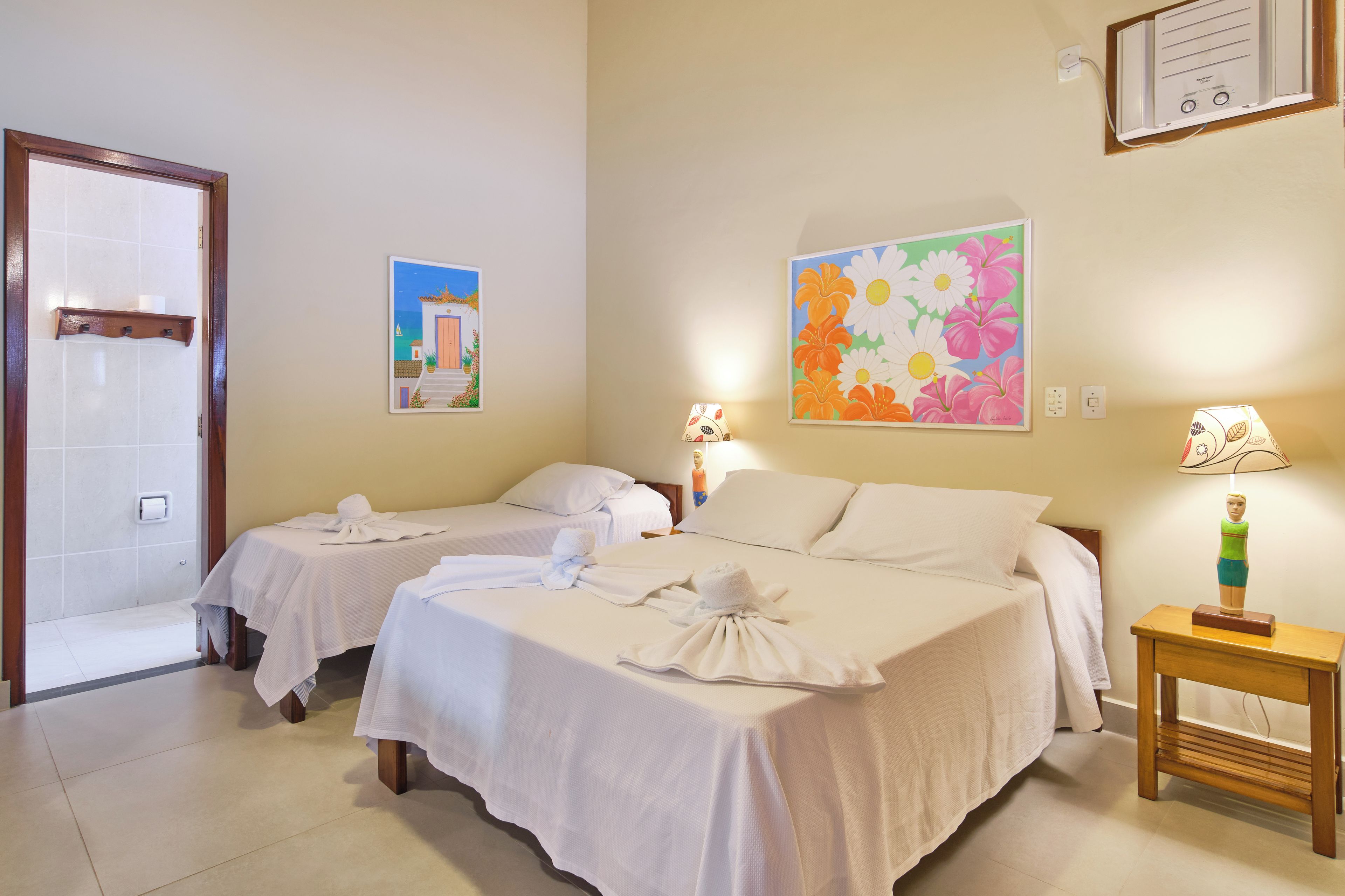 Quarto de hotel com duas camas, um quadro, um abajur e uma mesa de cabeceira de madeira.