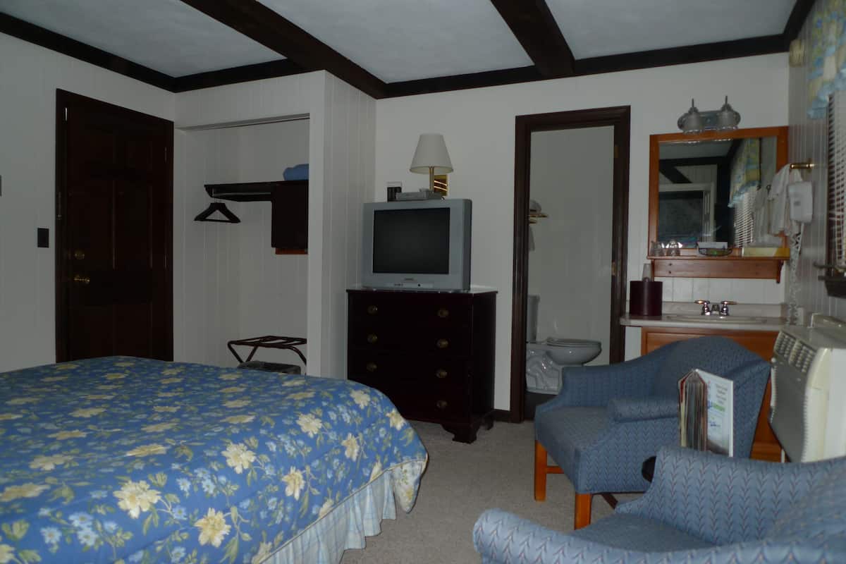 Quarto com cama, penteadeira, televisão, cadeira e espelho de banheiro.