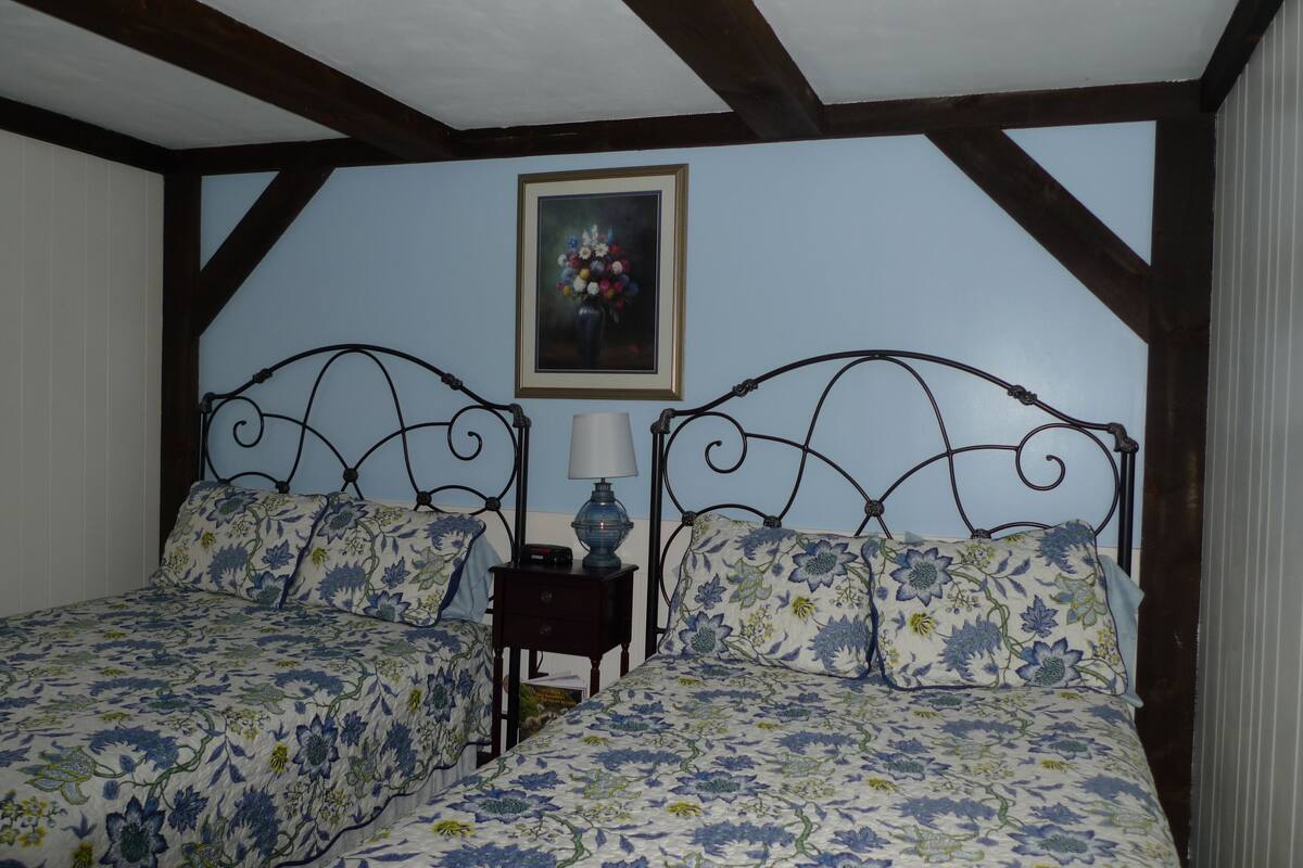 Quarto com duas camas, mesa de cabeceira com abajur e quadro emoldurado na parede.
