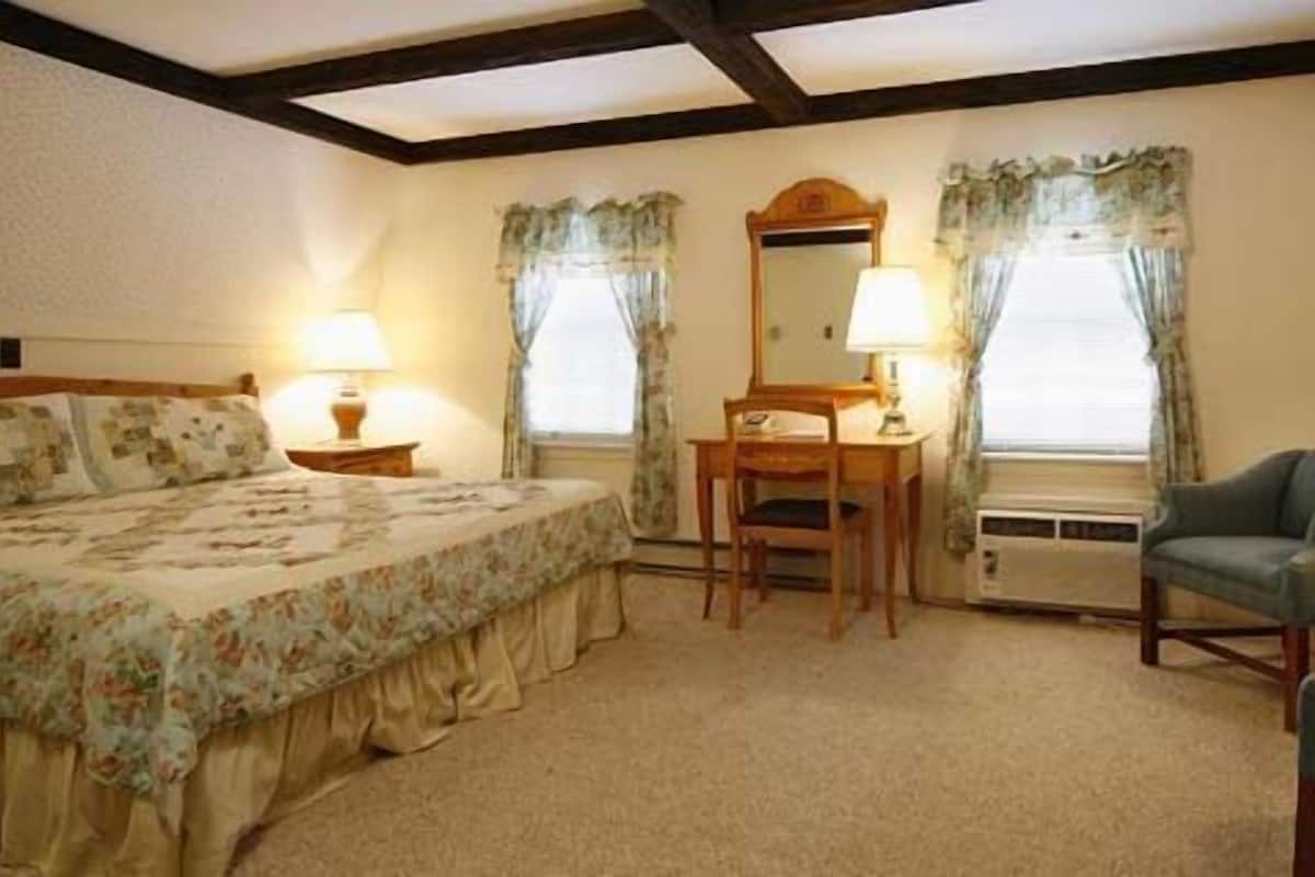 Um quarto com uma cama, uma escrivaninha, uma cadeira, um espelho e uma janela com cortinas.