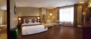 Quarto de hotel com uma cama grande, um sofá, uma escrivaninha e uma cadeira.