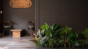 Uma área de recepção com uma placa de madeira que diz "WELLIES HOTEL Karuizawa", um banco, duas cadeiras e uma variedade de plantas verdes.