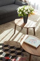 Uma sala de estar com sofá, uma mesinha de madeira com um livro e um vaso com flores brancas.