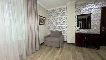 Um quarto com uma poltrona cinza, piso de madeira, papel de parede estampado, um espelho e uma porta.