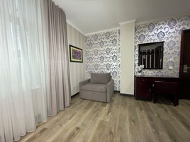 Um quarto com uma poltrona cinza, piso de madeira, papel de parede estampado, um espelho e uma porta.