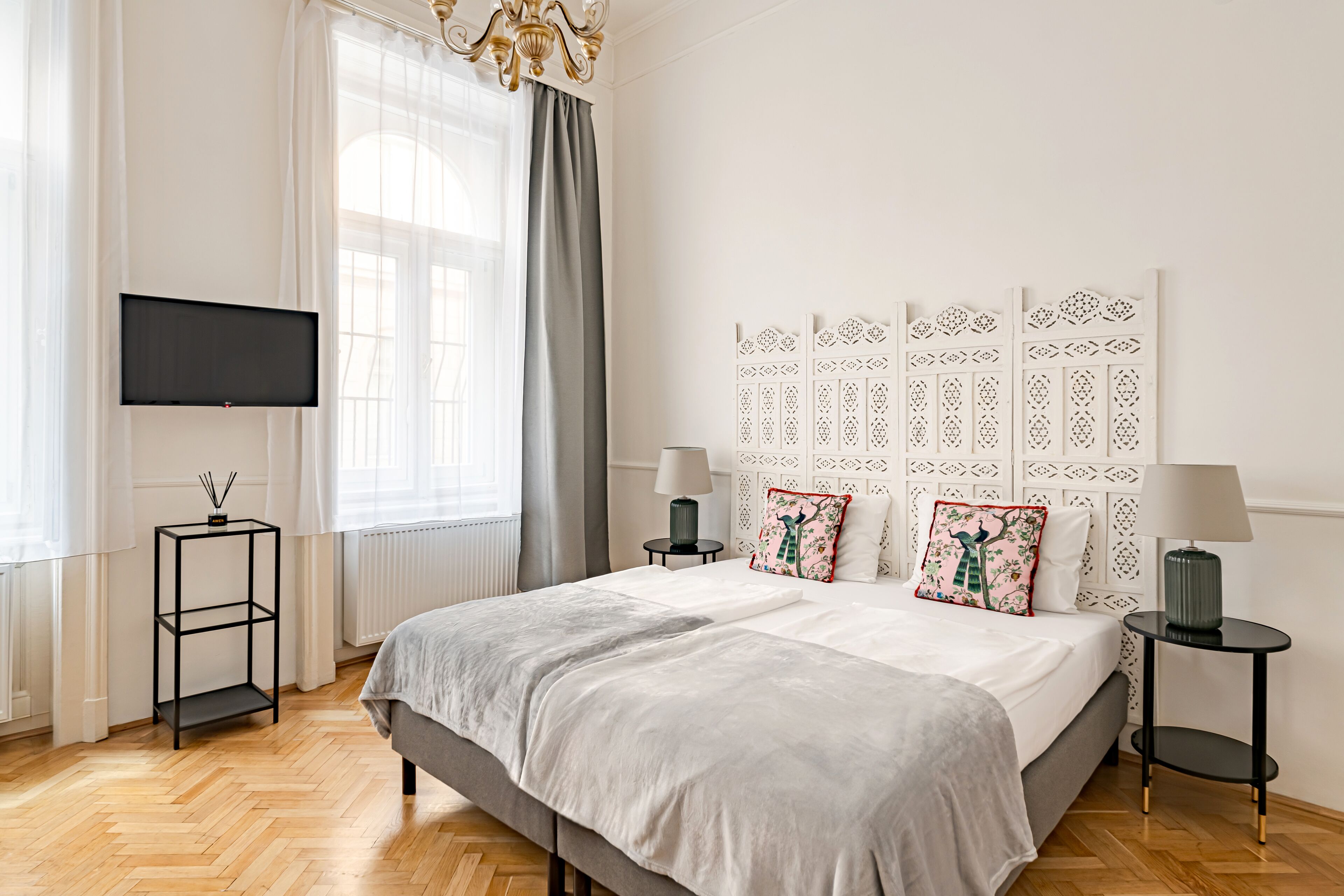 Quarto com cama grande, televisão na parede, cabeceira decorativa e mesa de cabeceira pequena.