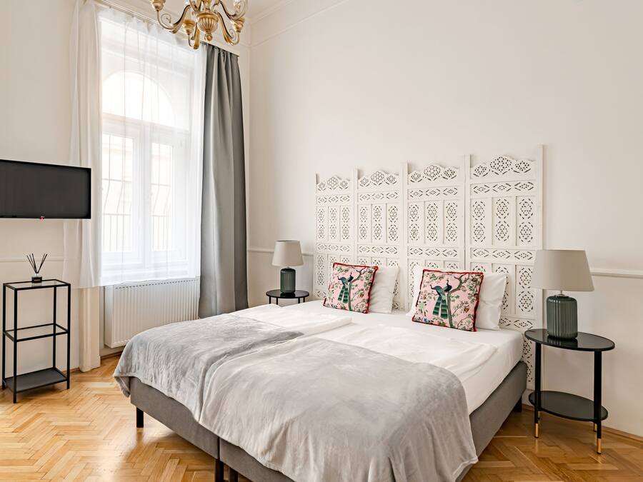 Quarto com cama grande, televisão na parede, cabeceira decorativa e mesa de cabeceira pequena.