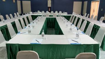 Uma sala de conferências com uma mesa comprida, cadeiras e garrafas de água.
