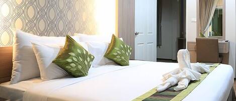 Cama bem arrumada com lençóis brancos e almofadas com padrão de folhas, uma toalha sobre a cama e papel de parede estampado na parede.