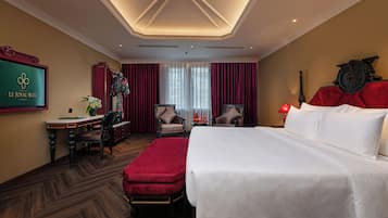 Quarto de hotel com cama, escrivaninha, cadeira, televisão e cortina vermelha.