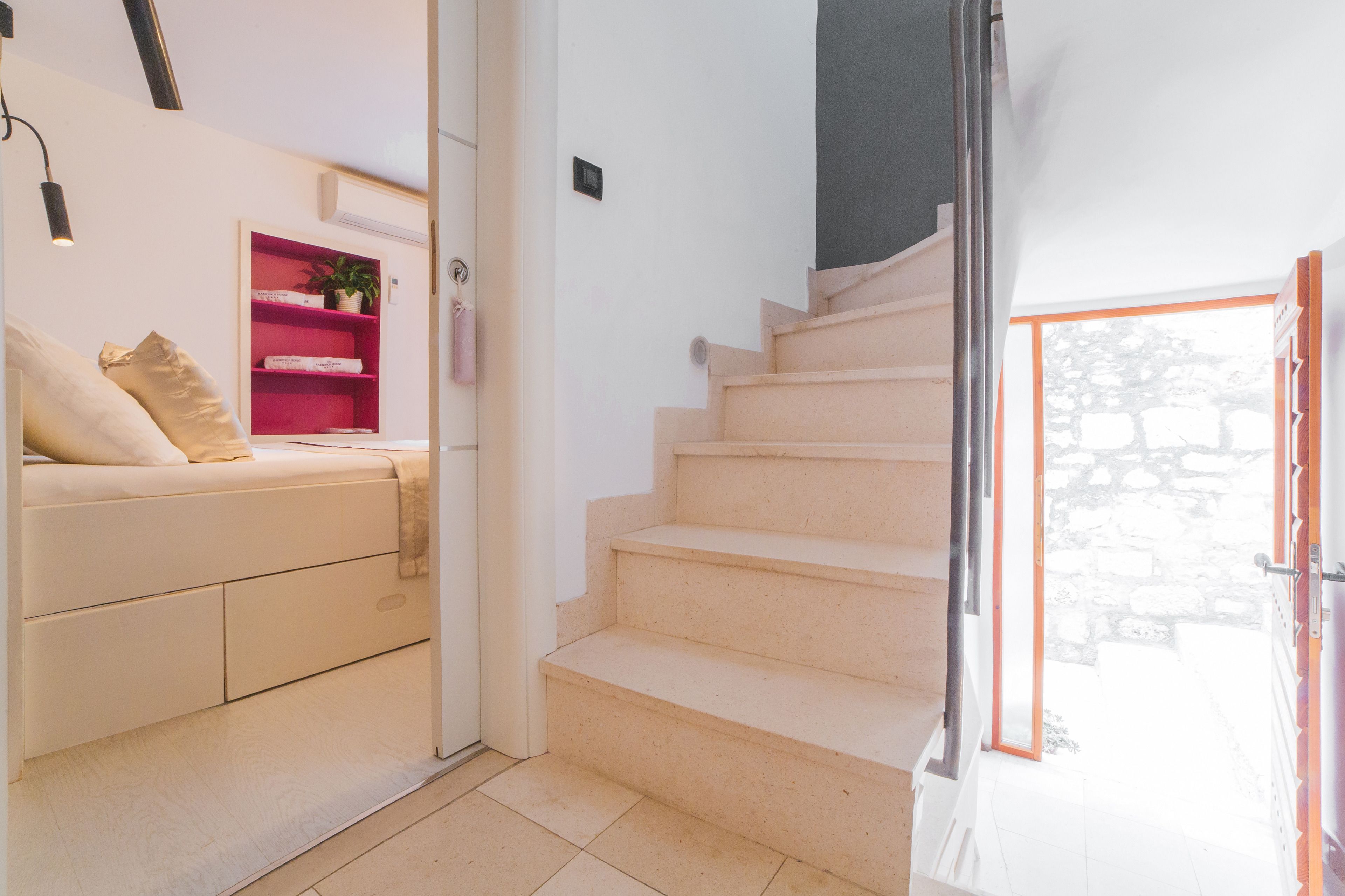 Interior moderno com escada para uma varanda, sofá com almofadas e um móvel estante rosa.