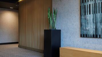 Um hall moderno com carpete estampado, uma grande planta em vaso, um balcão de recepção de madeira e um painel decorativo na parede.