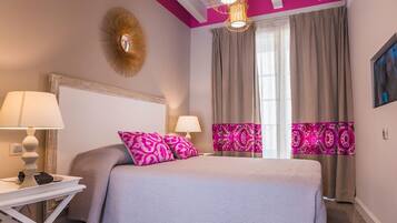 Quarto de hotel com uma cama, duas luminárias laterais, uma mesinha com abajur, um relógio de parede e um espelho grande.