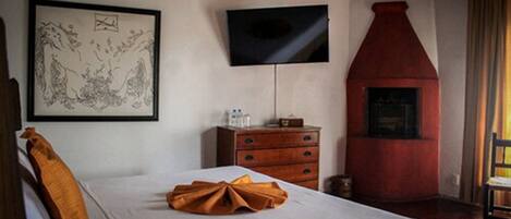 Quarto de hotel com uma cama, televisão de tela plana, cômoda de madeira, lareira vermelha e uma obra de arte emoldurada na parede.