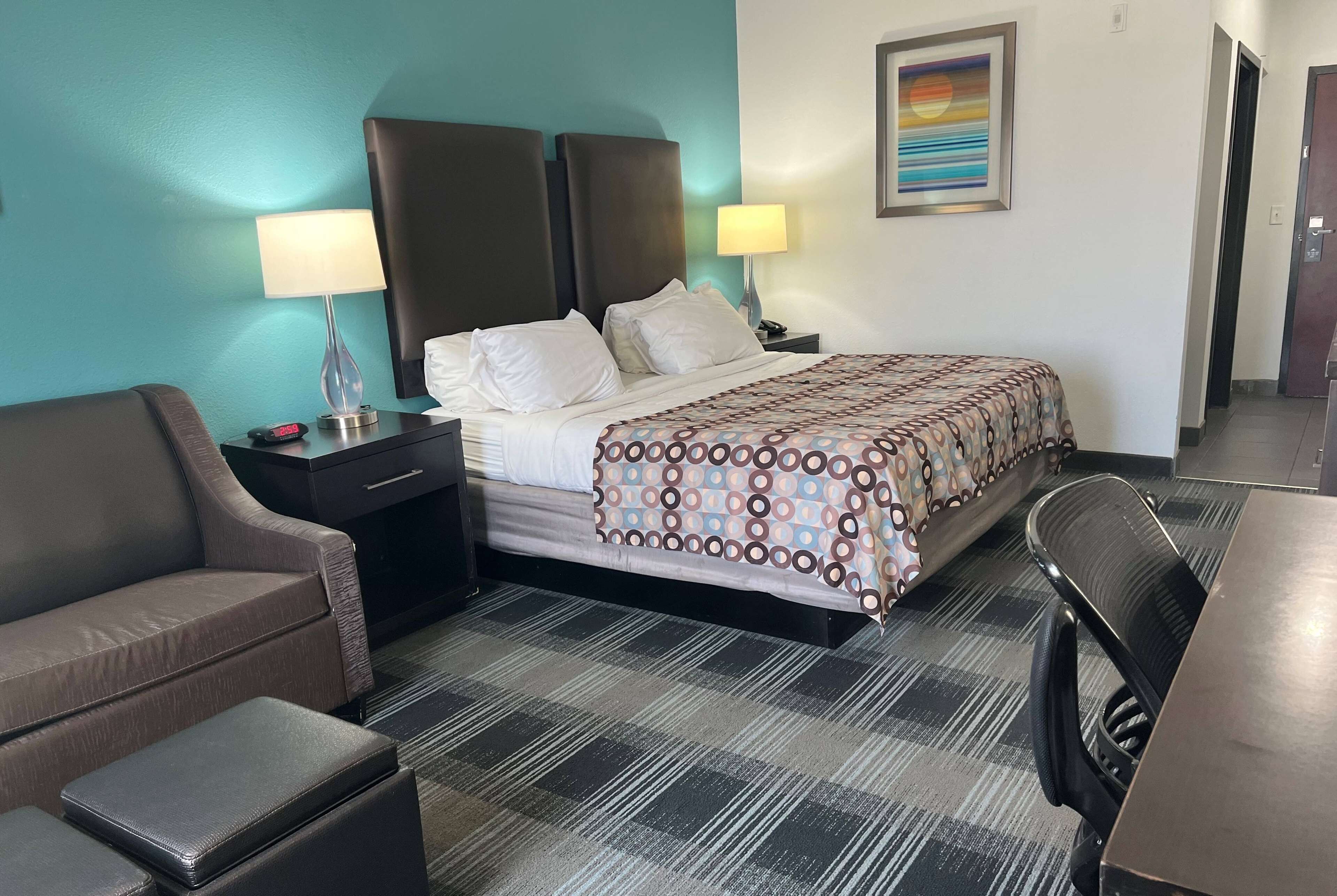 Quarto de hotel com cama, escrivaninha, cadeira e sofá.