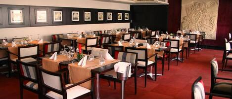 Uma sala de jantar formal com várias mesas e cadeiras, obras de arte nas paredes e um grande painel decorativo.
