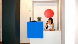 Uma mesa de recepção com um painel azul, uma decoração circular vermelha na parede e um vaso de planta.