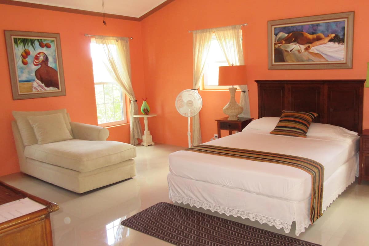 Um quarto com cama, uma cadeira, um ventilador e obras de arte nas paredes.