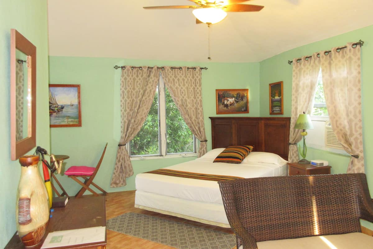 Quarto com cama, escrivaninha, cadeira, mesa de cabeceira e ventilador de teto.