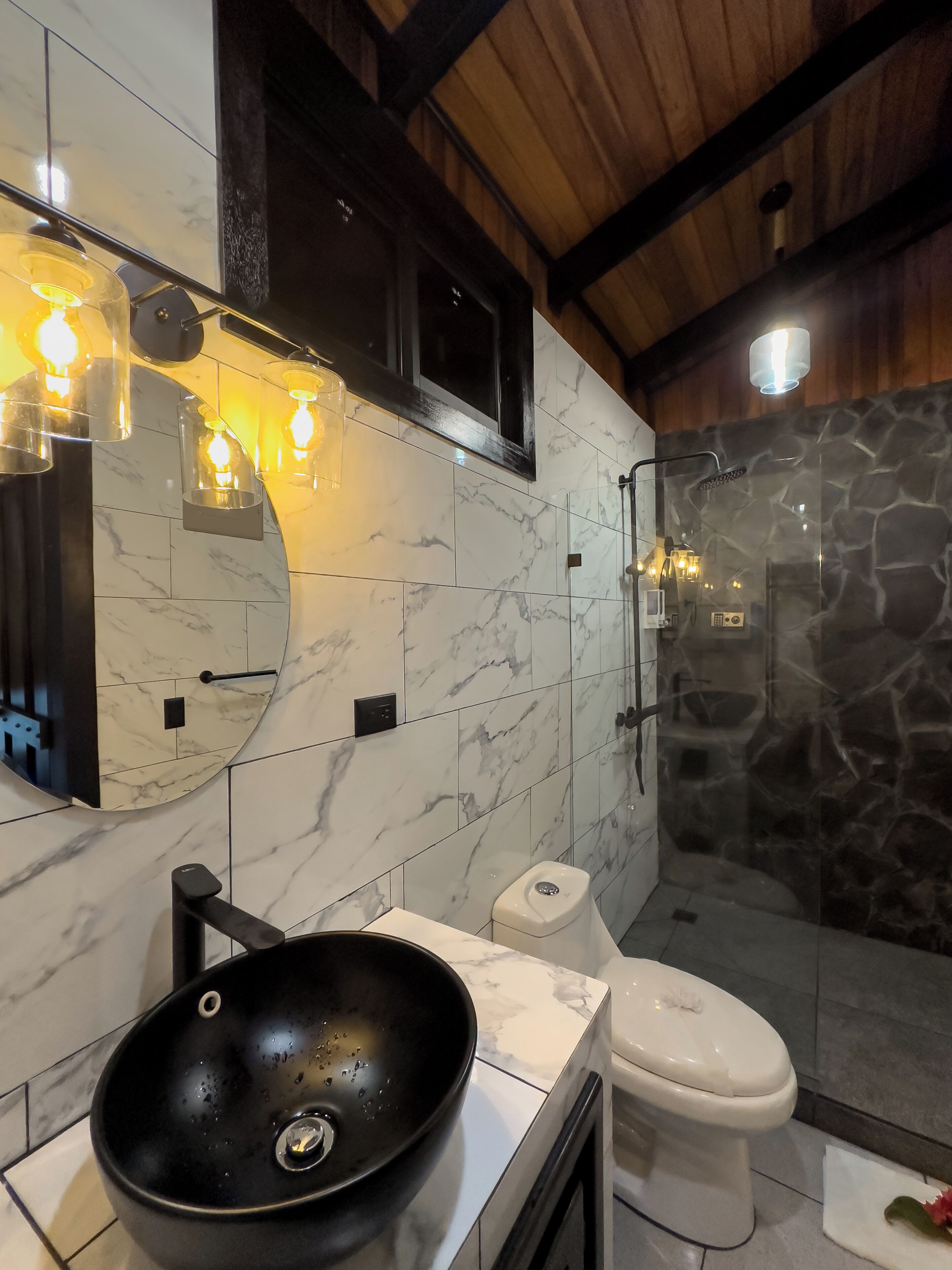 Uma casa de banho moderna com lavatório preto, sanita branca e cabine de duche em vidro.