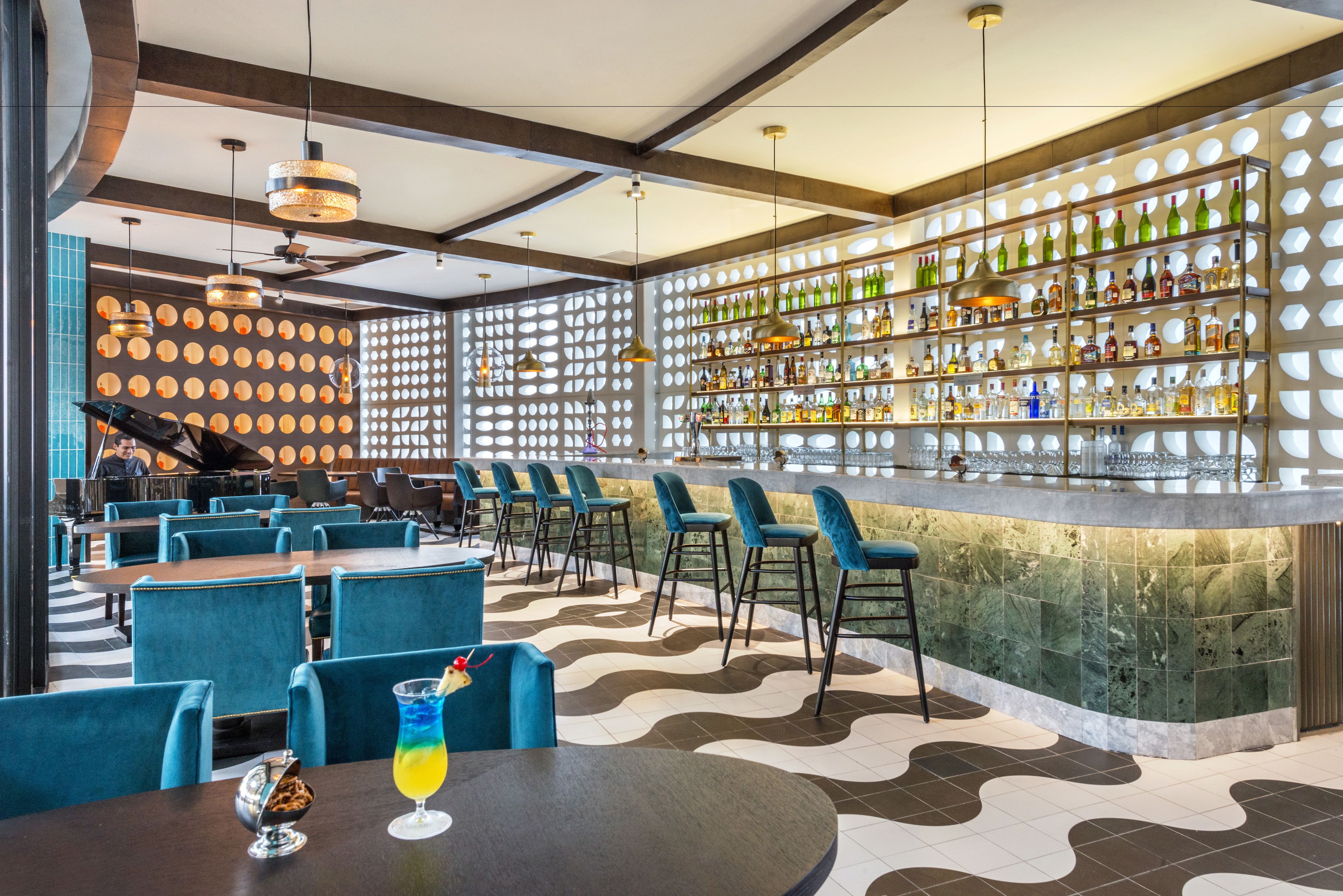 Uma área de bar com cadeiras azuis, um balcão com garrafas e um chão estampado.