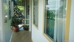 Corredor estreito com planta em vaso, corrimão de metal decorativo e uma grande janela com vista para áreas verdes e edifícios.