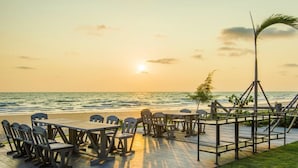 Um restaurante à beira-mar com mesas ao ar livre e vista para o oceano ao pôr do sol.