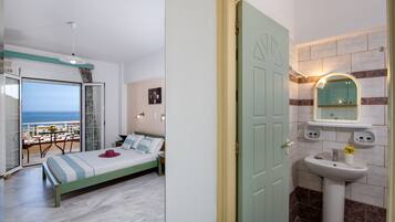 Quarto com cama, vista para o mar, banheiro com pia e espelho, e porta que dá para outro cômodo.