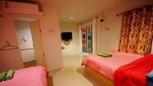 Quarto de hotel com duas camas, uma televisão, banheiro com chuveiro e cortina estampada.