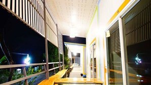 Um corredor com um banco de madeira, corrimão de metal e uma porta de vidro que dá para um quarto.