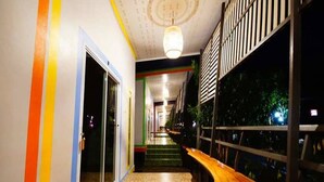 Um corredor com um banco de madeira, uma escadaria e vista para o exterior à noite.