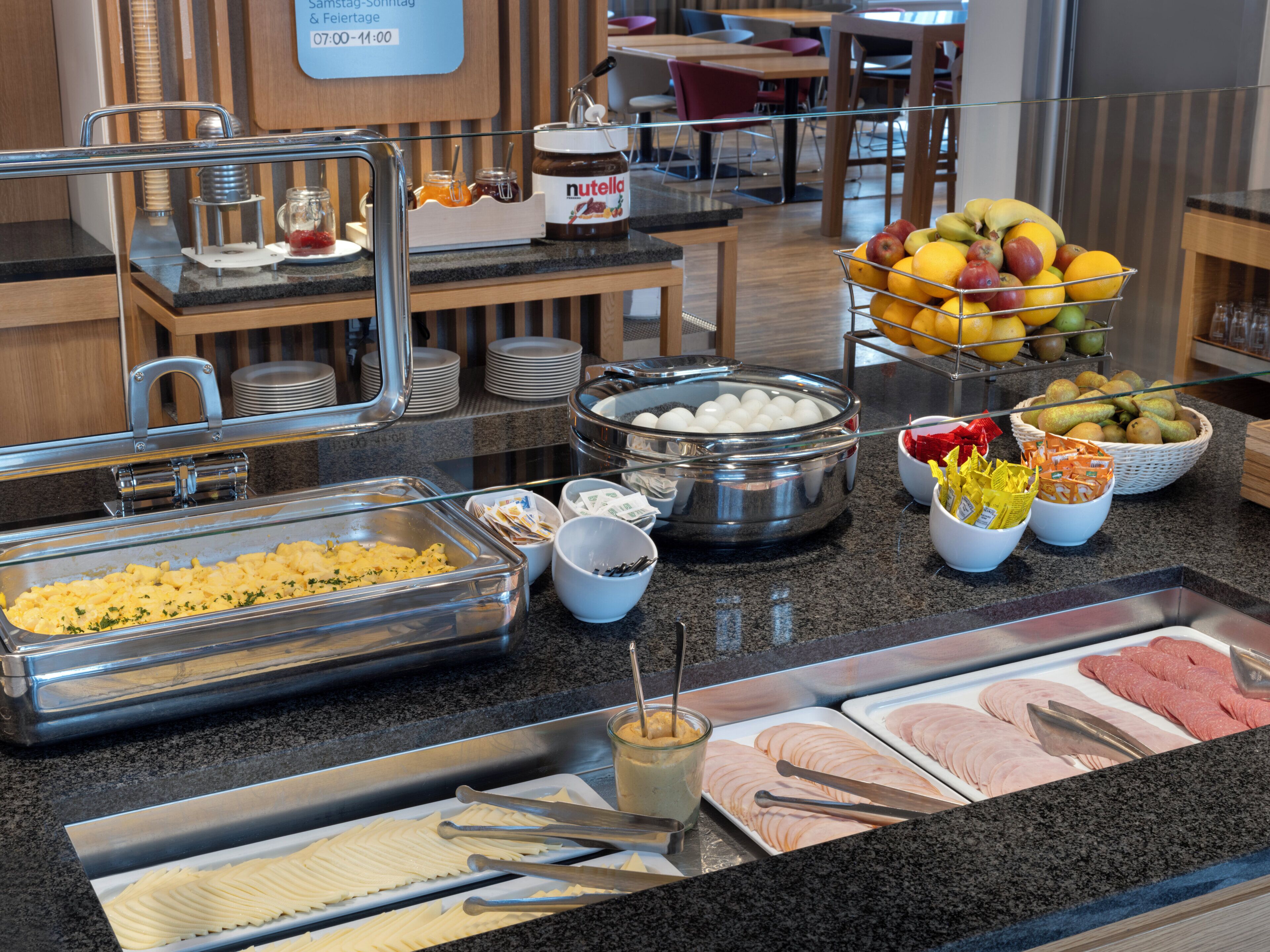 Espaço de buffet com diversas opções de comida, incluindo ovos, carnes e frutas.