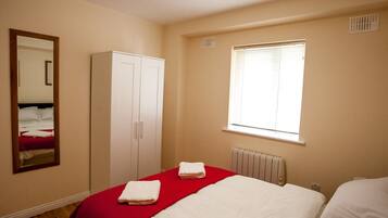Quarto com cama, guarda-roupa, janela com persianas e radiador.