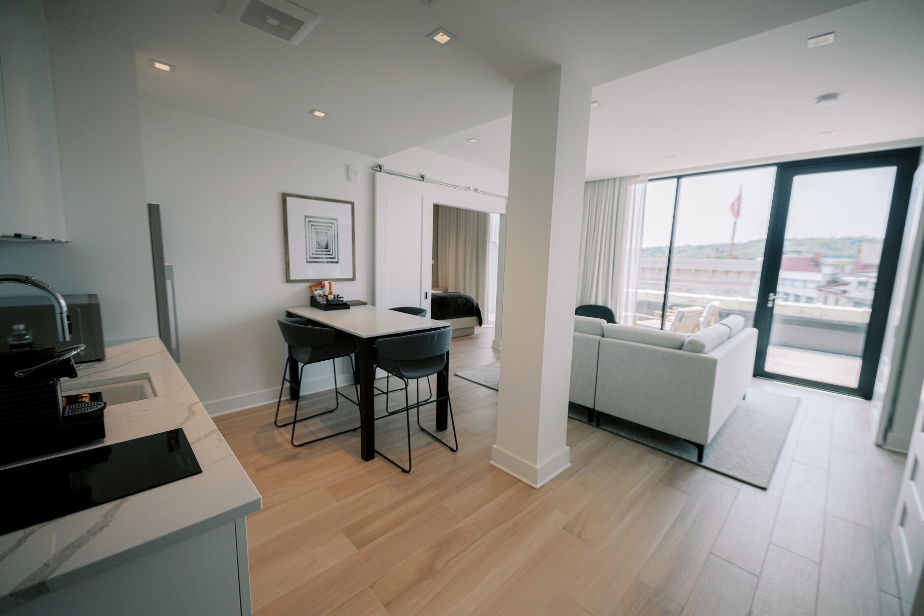 Quarto de hotel moderno com área de refeições, sofá e uma grande janela com vista para a cidade.