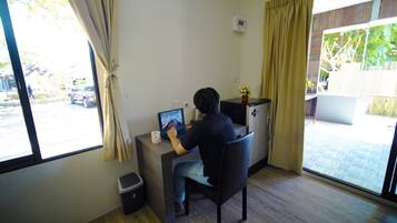 Um quarto com escrivaninha, cadeira, laptop, chávena de café e janela com cortinas.
