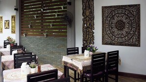 Uma área de refeições com mesas preparadas para dois, com toalhas de mesa estampadas e cadeiras de madeira escura.