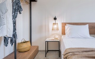 Quarto com cama, mesa de cabeceira com um livro, luminária pendente e cesta de vime em um banco.