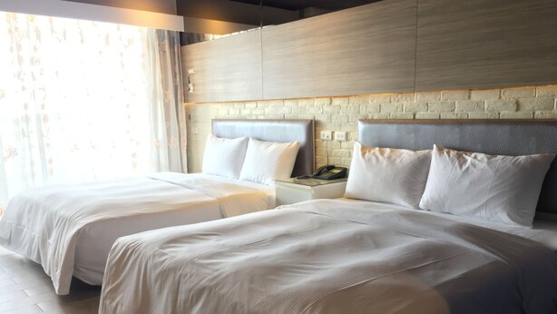 Quarto de hotel com duas camas, parede de tijolos e mesa de cabeceira com telefone.