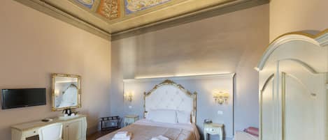 Quarto de hotel com uma cama grande, uma escrivaninha com cadeira, televisão fixada na parede e uma porta.