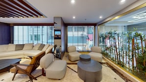 Uma sala de estar moderna com sofá em formato de L, poltronas, mesa de centro e uma grande janela com vista para a cidade.