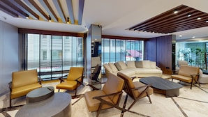 Um lobby moderno com um sofá modular, poltronas de couro, uma mesa de centro e janelas amplas com persianas.