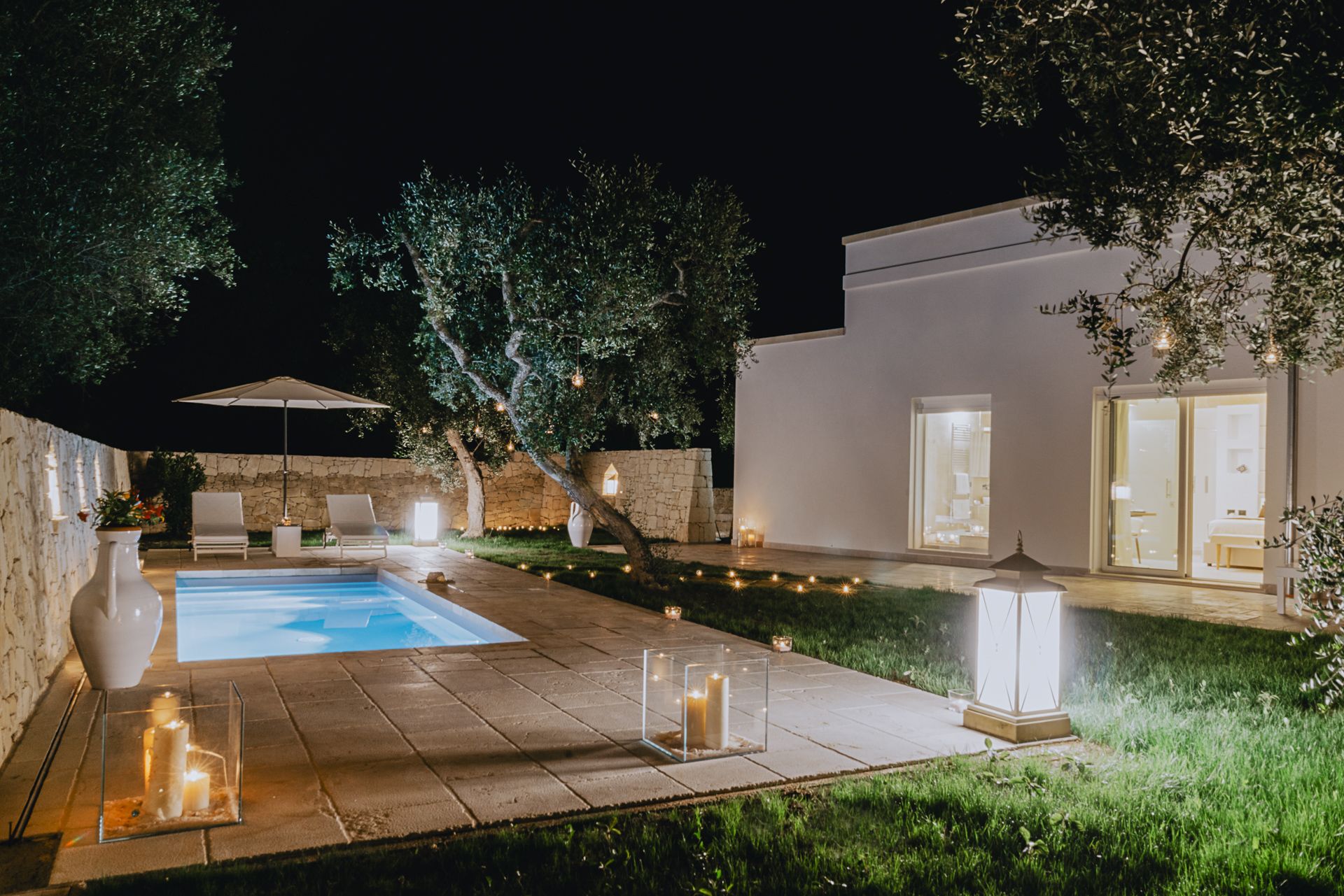 Uma área moderna de piscina ao ar livre, com um muro de pedra, espreguiçadeiras e um caminho bem iluminado.