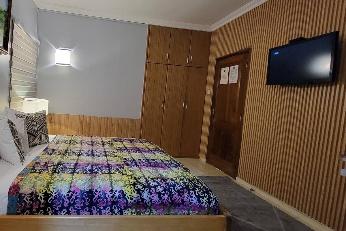 Quarto com cama, mesa de cabeceira, luminária, televisão e armários de madeira.