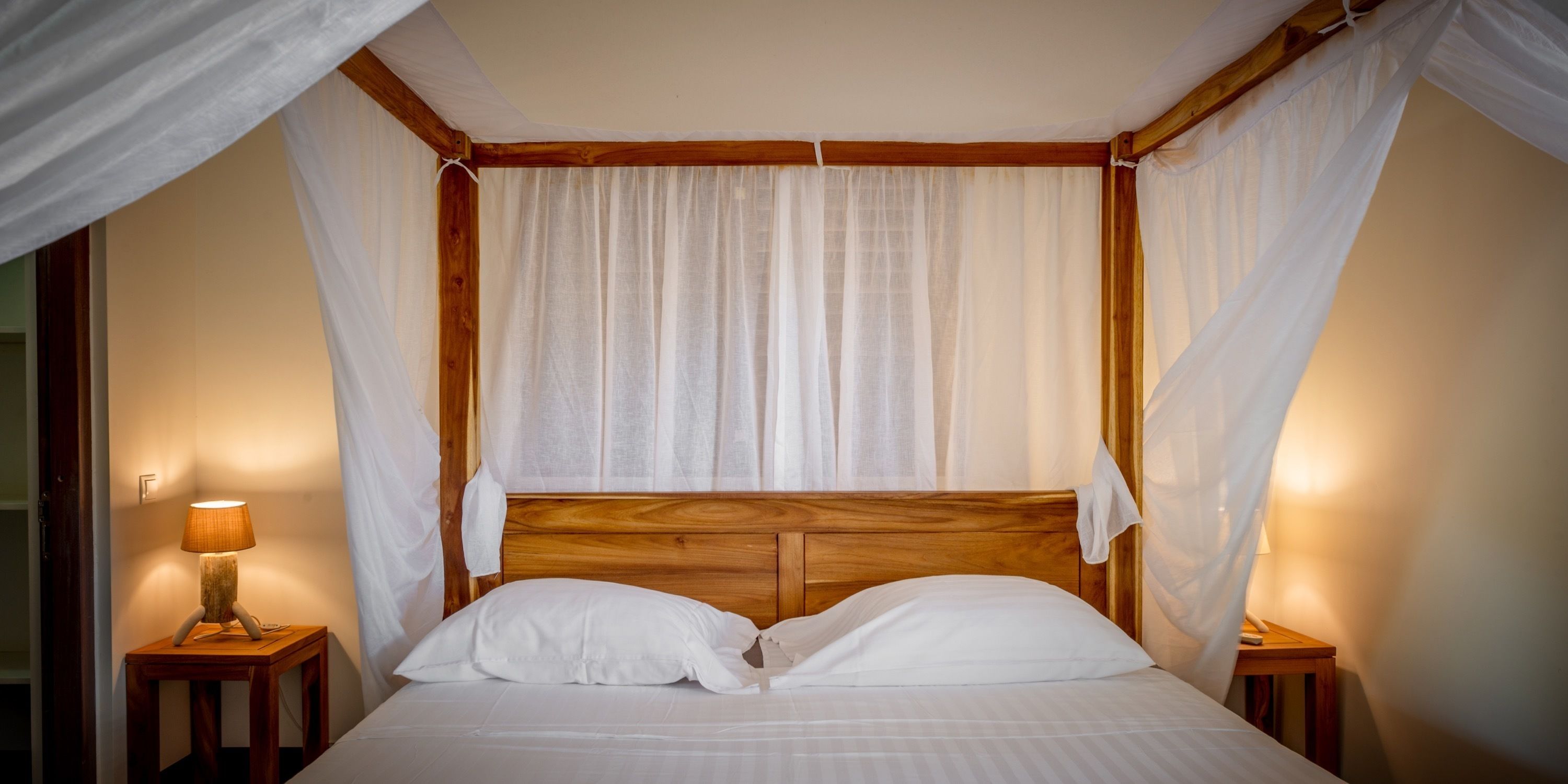 Quarto com cabeceira de madeira, roupa de cama branca e luminária de cabeceira.