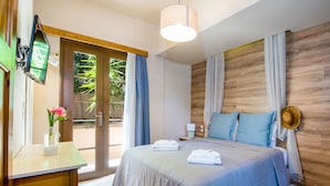 Quarto de hotel com cama, escrivaninha, televisão e vista para o verde lá fora.