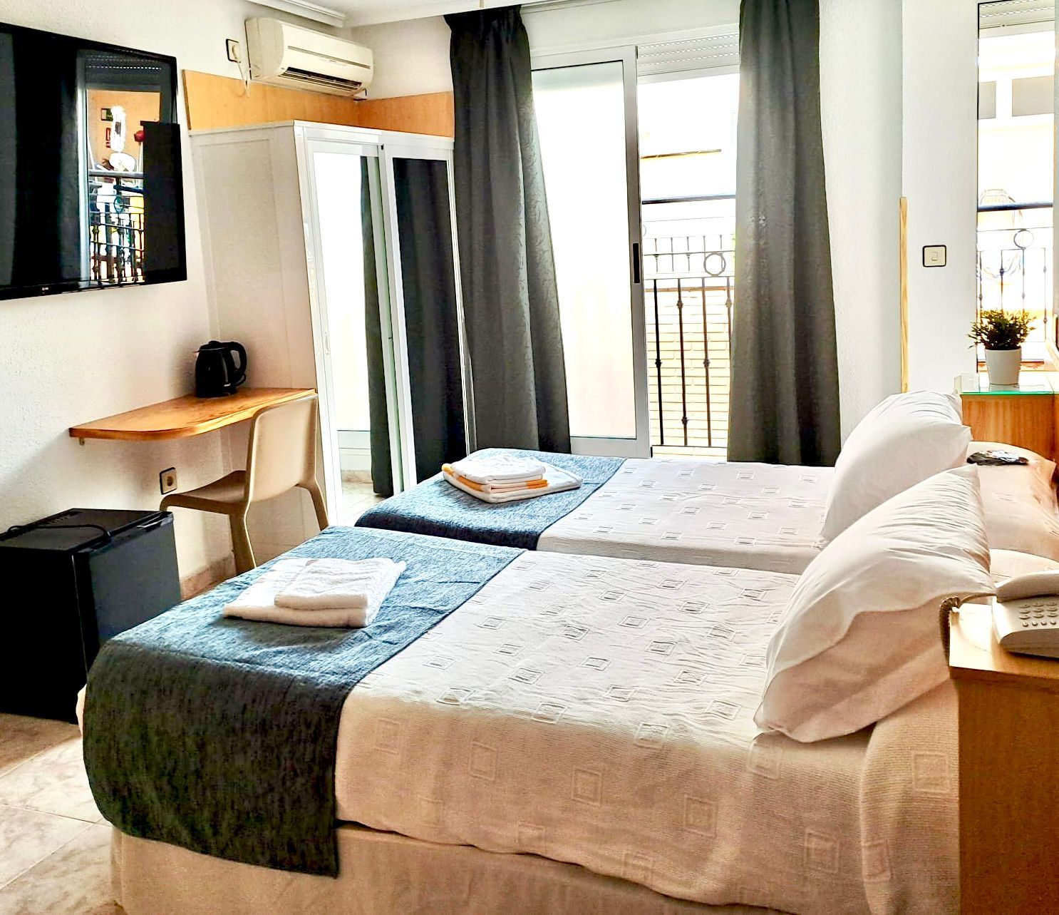Quarto de hotel com duas camas, uma escrivaninha, uma cadeira, ar condicionado e vista para o exterior.