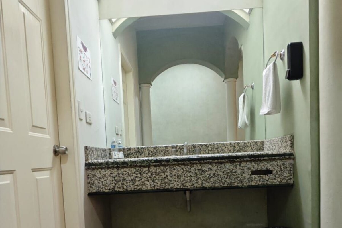 Casa de banho com bancada de granito, um cesto de lixo e porta-toalhas.