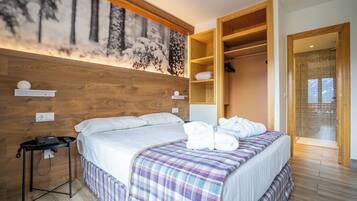 Quarto de hotel moderno com cabeceira de madeira, cama com manta xadrez, mesa de cabeceira com telefone, cabideiro e guarda-roupa.