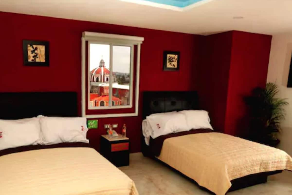 Quarto com duas camas, janela com vista para um edifício e paredes vermelhas.